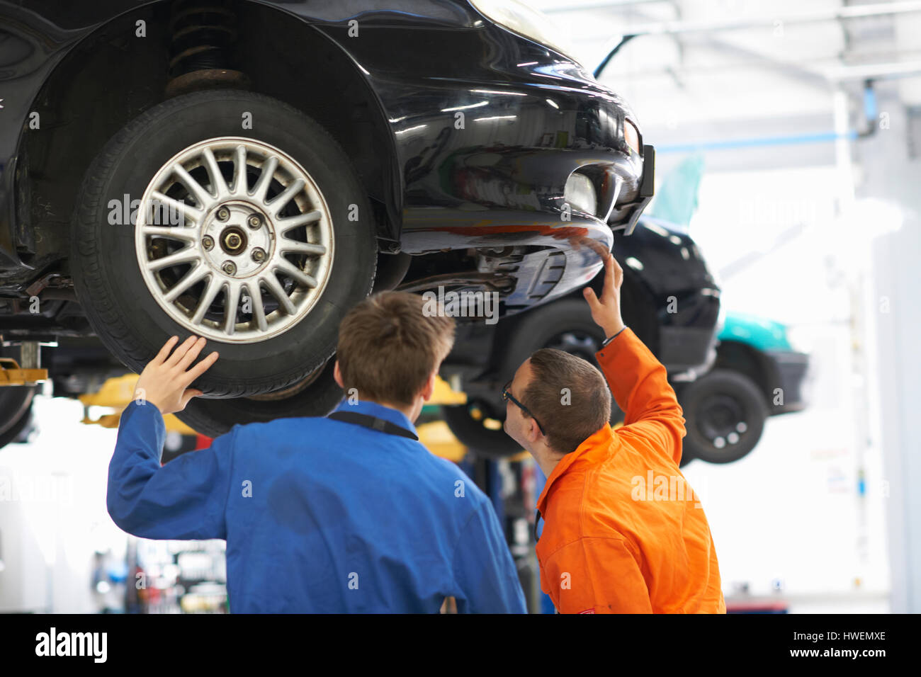Rear view of college mechanic students inspecting underneath of car ...