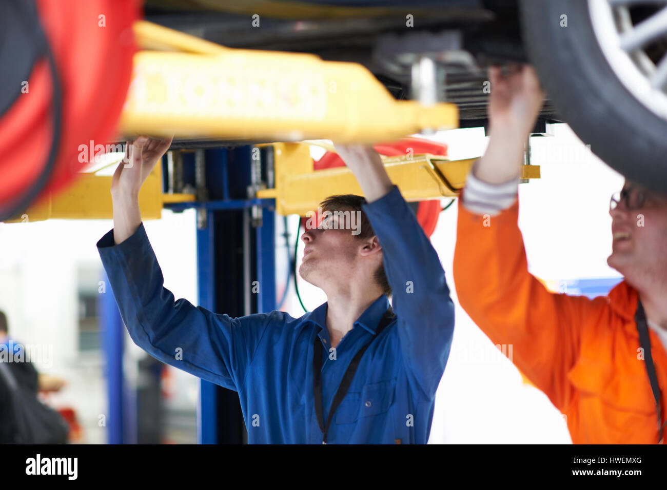 College mechanic students inspecting underneath car in repair garage ...