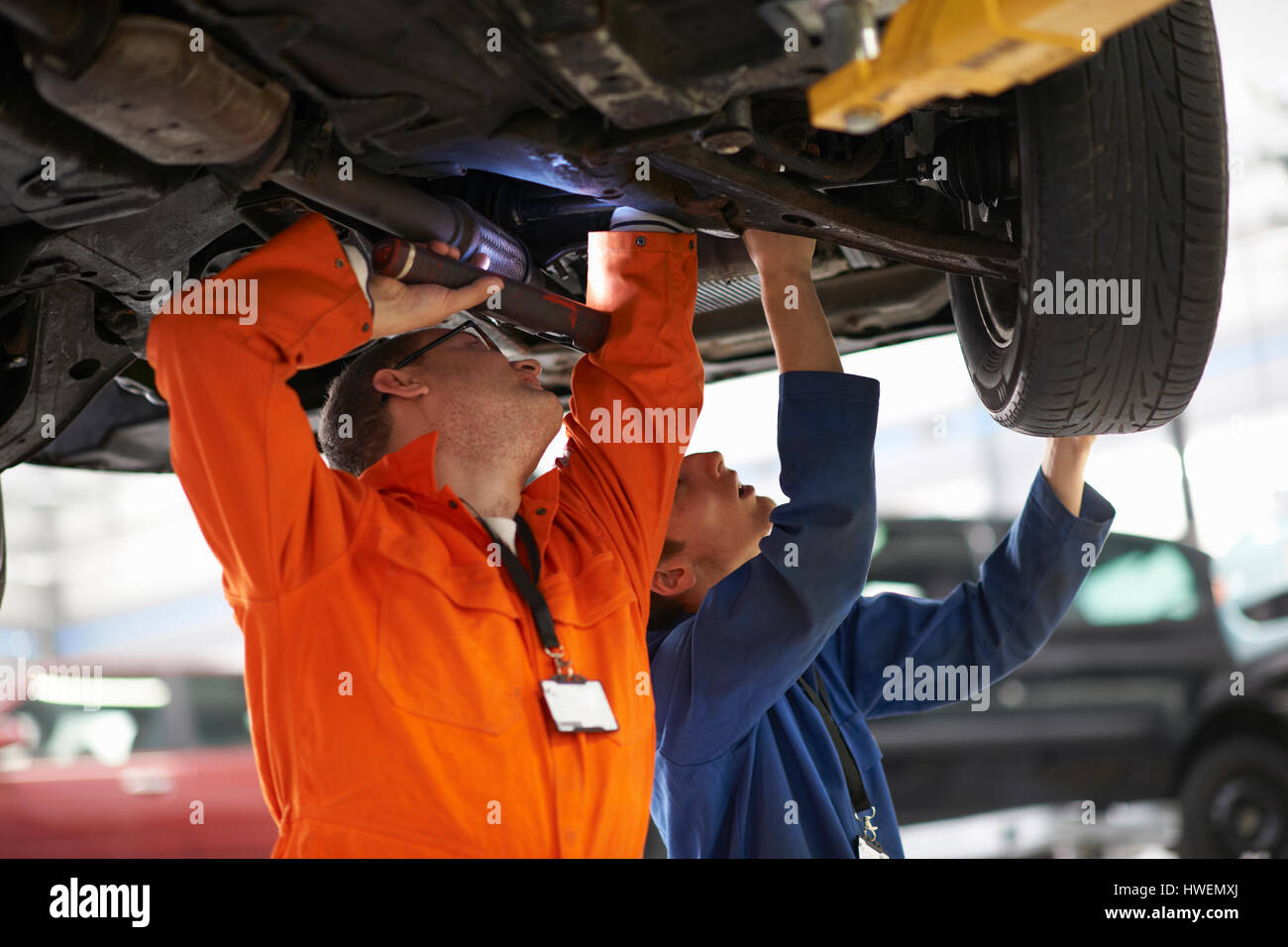 College mechanic students inspecting underneath car in repair garage ...