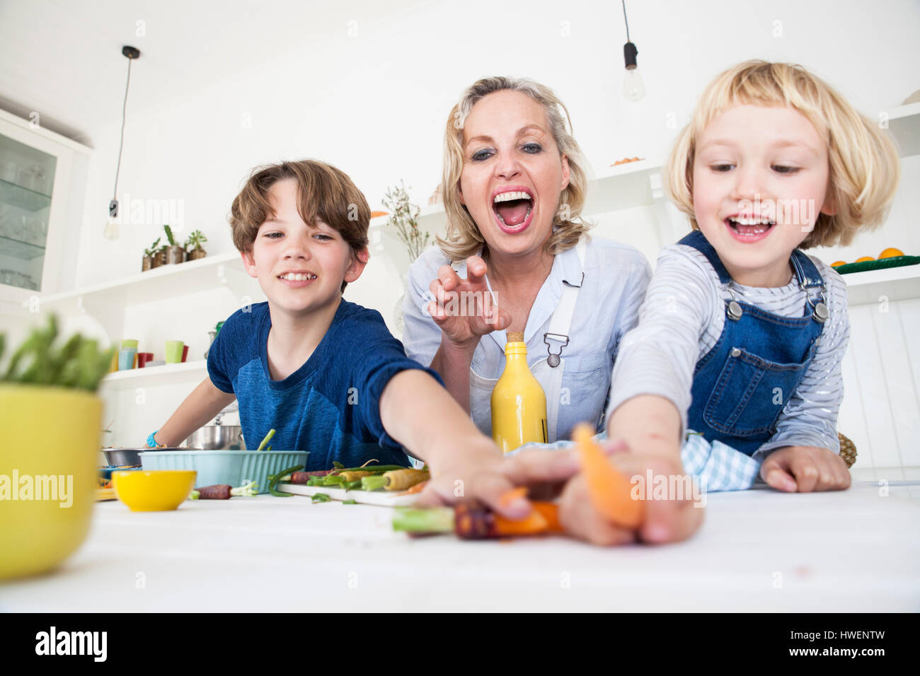 Girl and brother reaching for vegetable while preparing food at kitchen ...