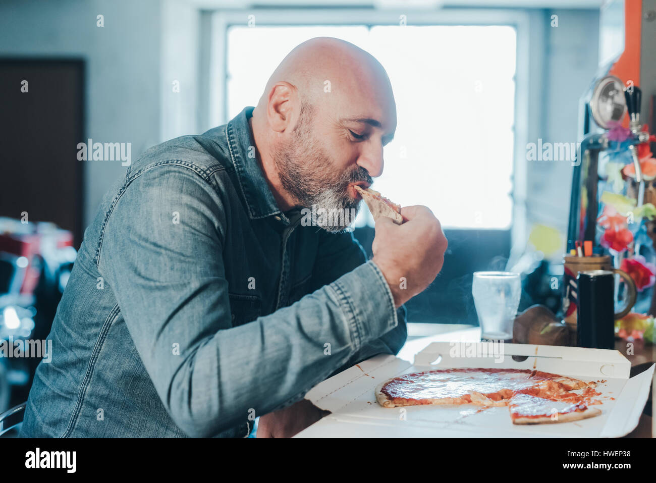 Mature man, sitting at table, eating takeaway pizza Stock Photo - Alamy