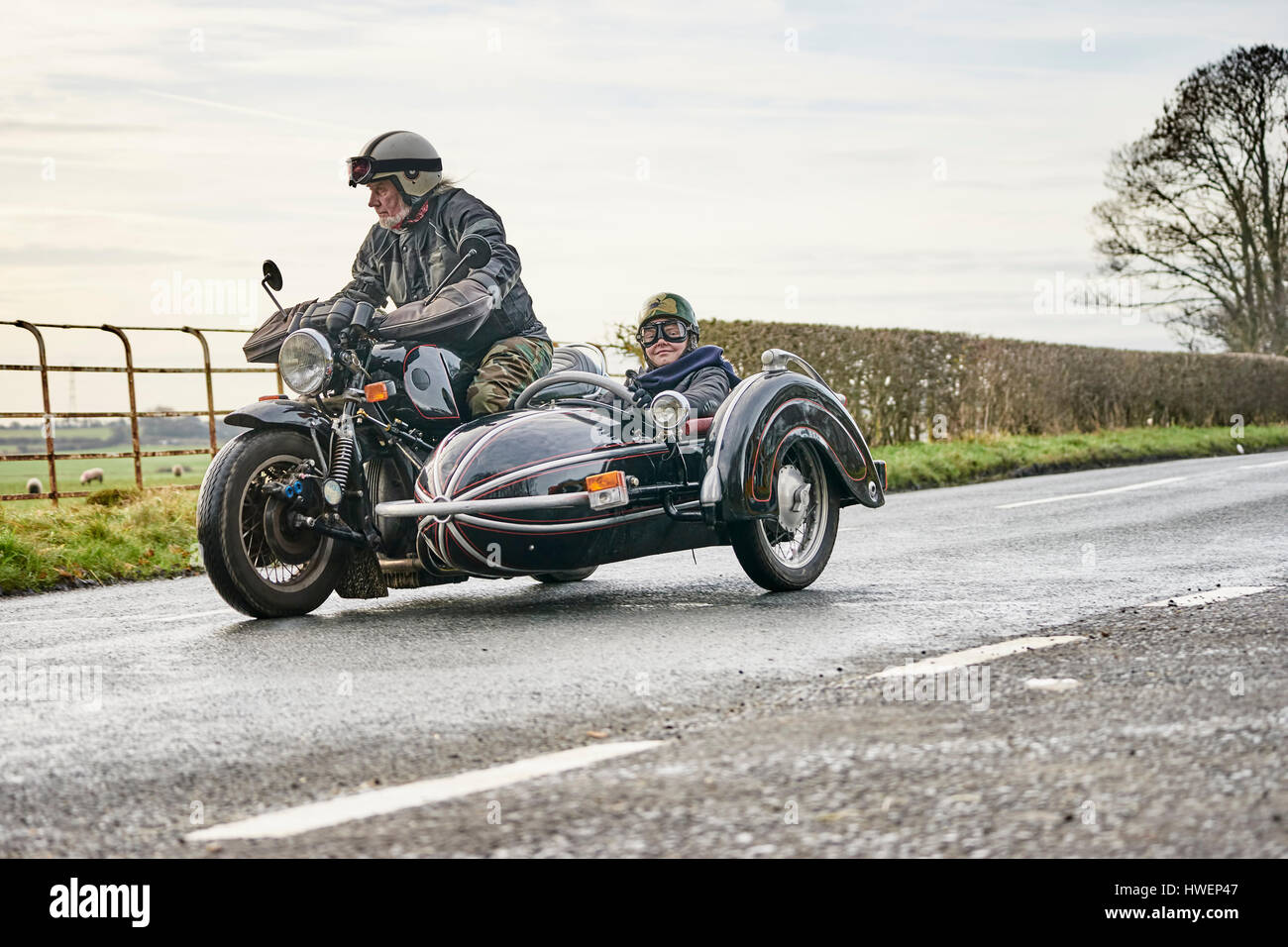 Senior man and grandson riding motorcycle and sidecar along rural road ...
