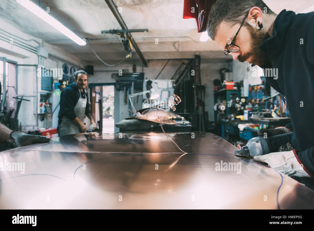 Metalworker gouging sheet copper at forge workbench Stock Photo - Alamy