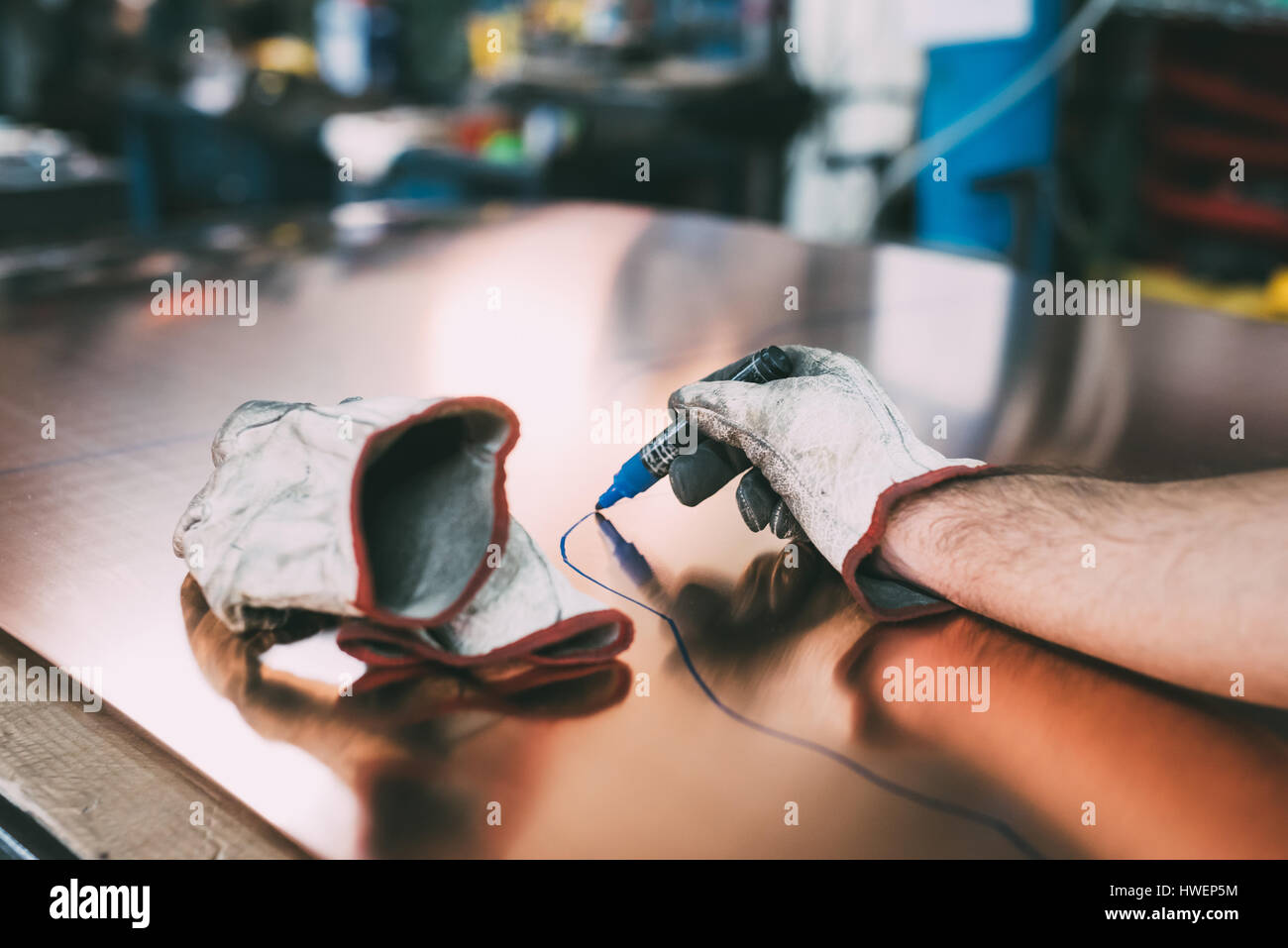 Hands of metalworker drawing outline on sheet copper at forge workbench ...