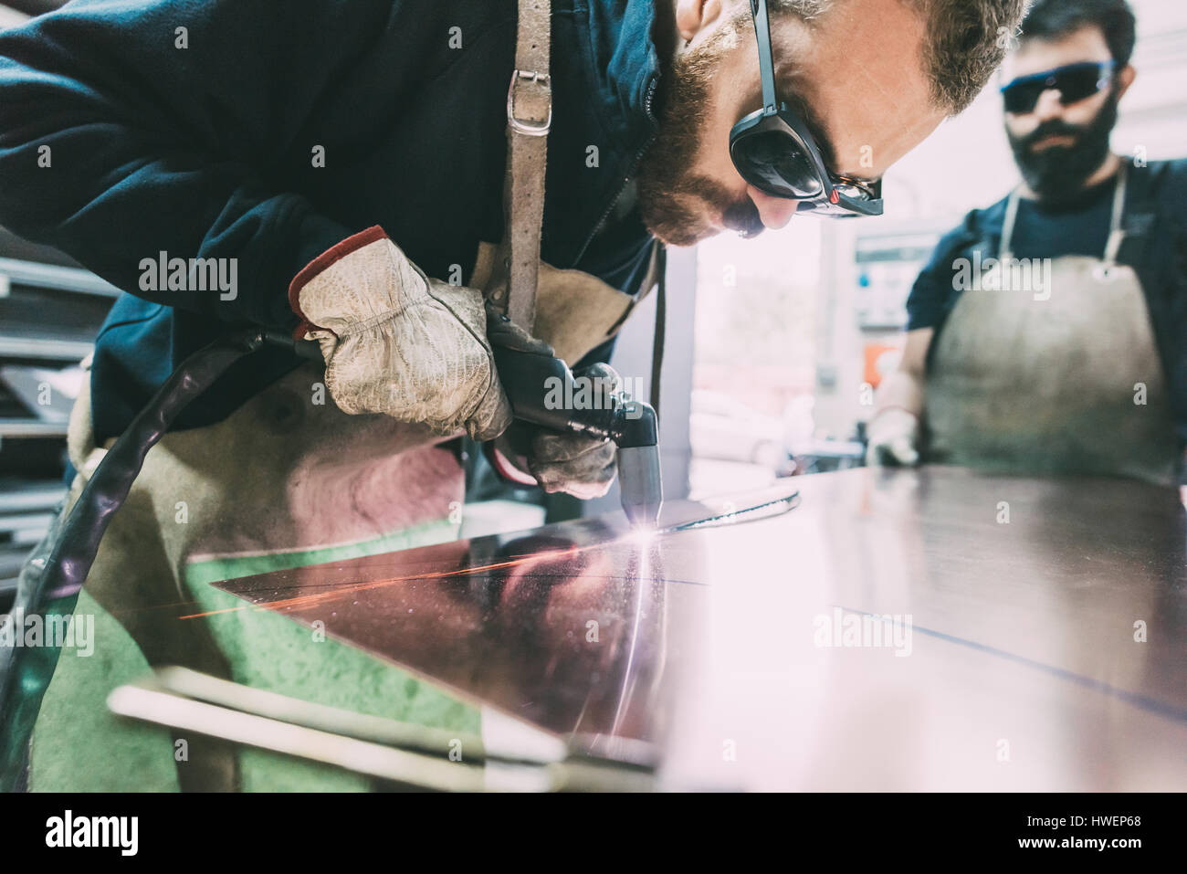 Metalworker cutting copper sheet with welding torch in forge workshop ...