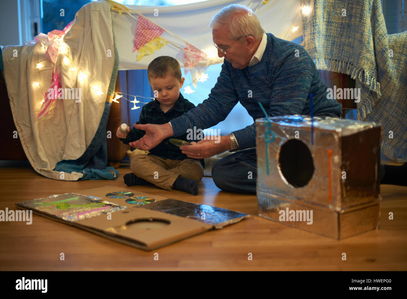Boy and grandfather sitting on floor making robot costume Stock Photo ...