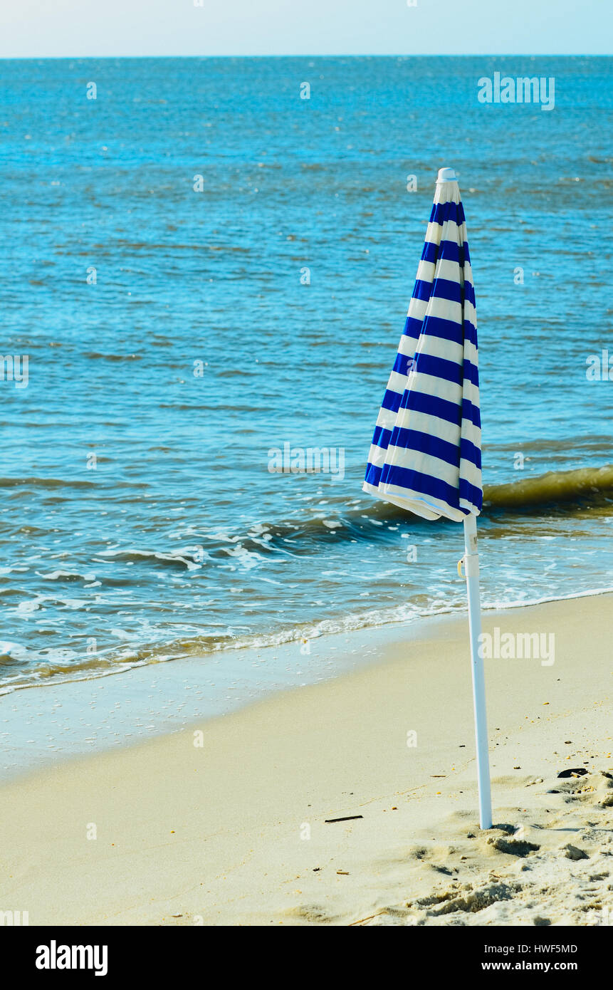 A white and blue stripped beach flag in the sand close to the water ...