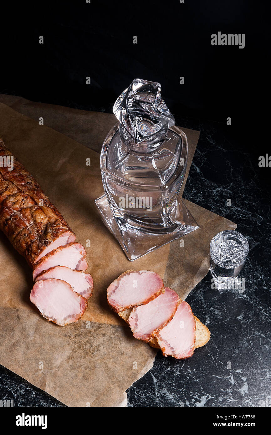 Bottle and shot glasses with vodka. Slices of smoked meat or ham on ...