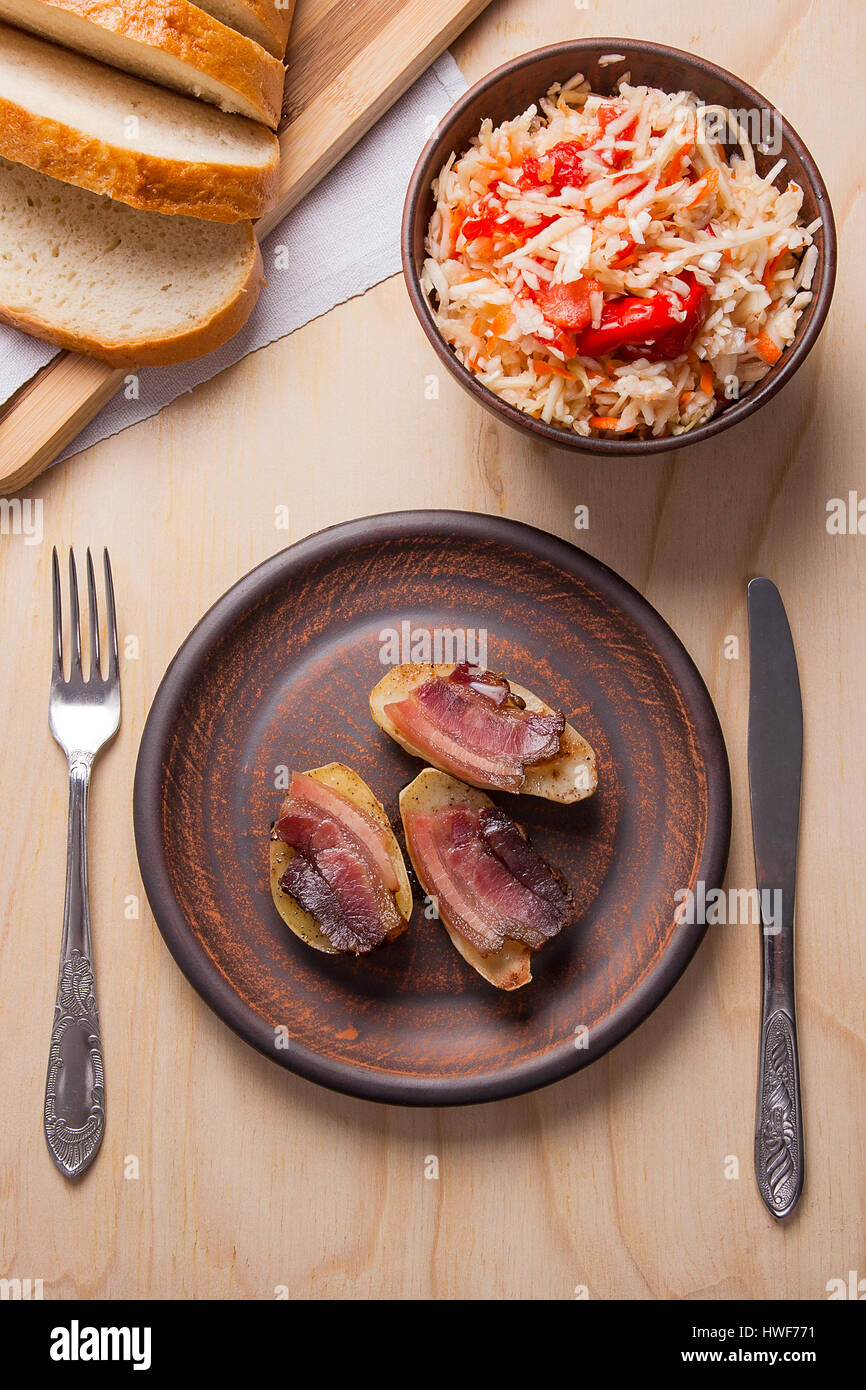 Tasty baked potatoes with slices of bacon in brown clay plate and ...