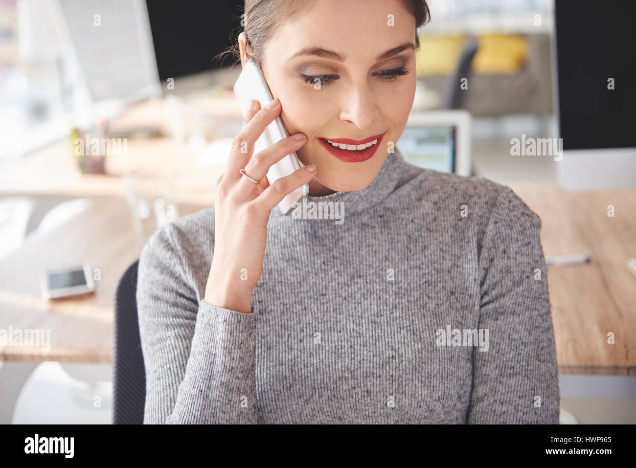 Smiling female using phone at her desk Stock Photo - Alamy
