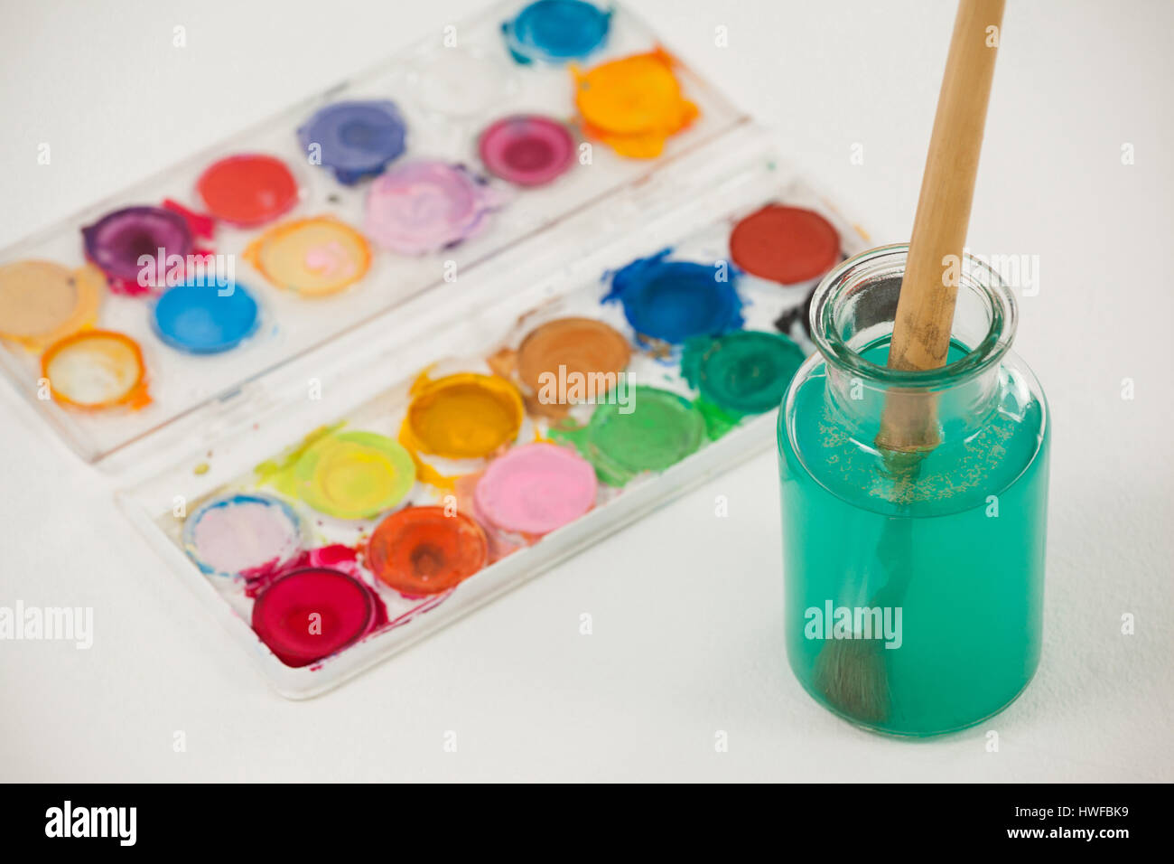 Watercolor palette and paint brush with blue paint dipped into water ...