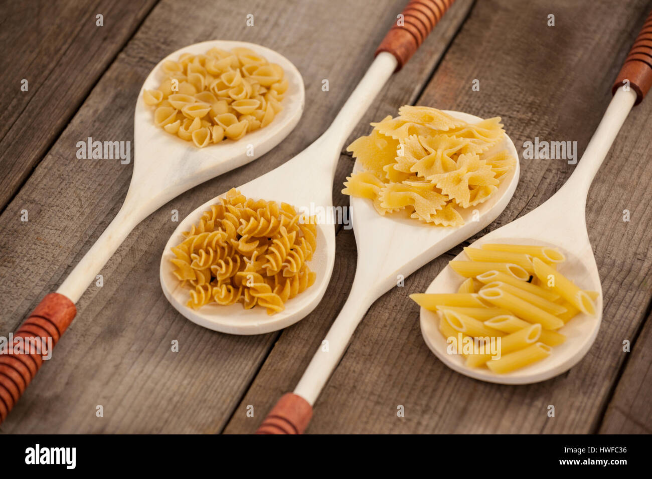 Spoons filled with varieties of pasta on wooden background Stock Photo ...