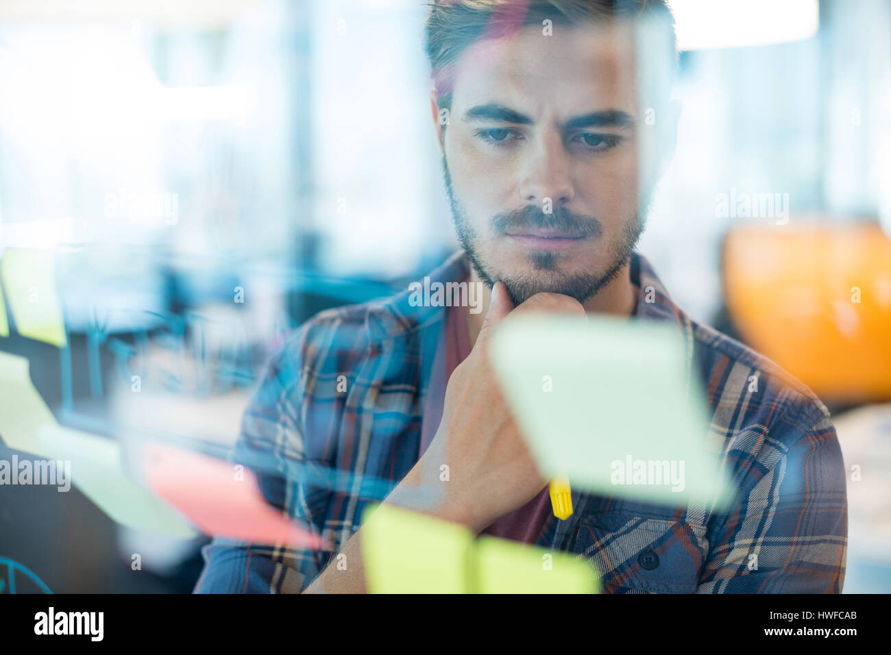 Thoughtful man reading sticky notes on the glass wall in office Stock ...