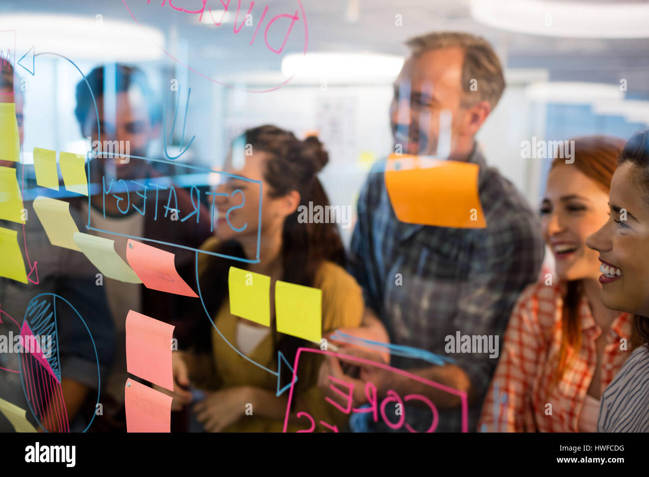 Creative business team looking at sticky notes on glass window in ...