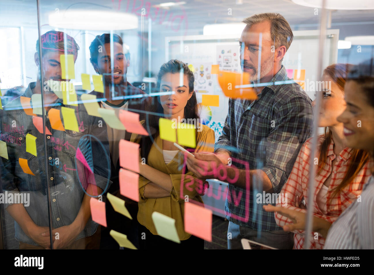 Creative business team looking at sticky notes on glass window in ...