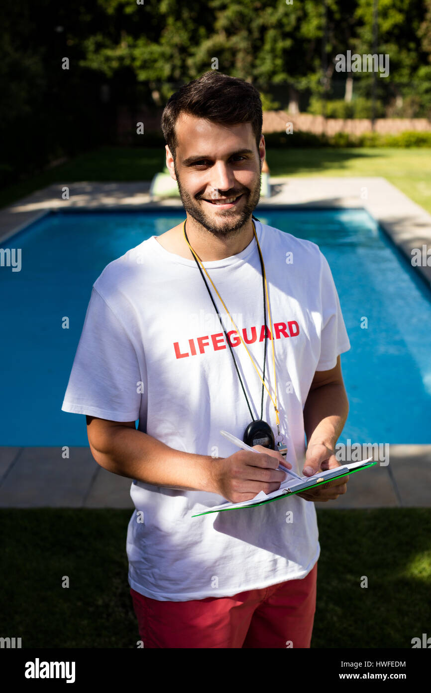 Portrait of lifeguard writing on clipboard at poolside on a sunny day ...