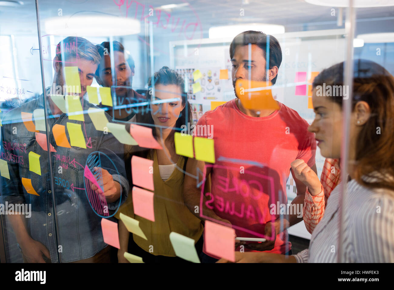 Creative business team looking at sticky notes on glass window in ...