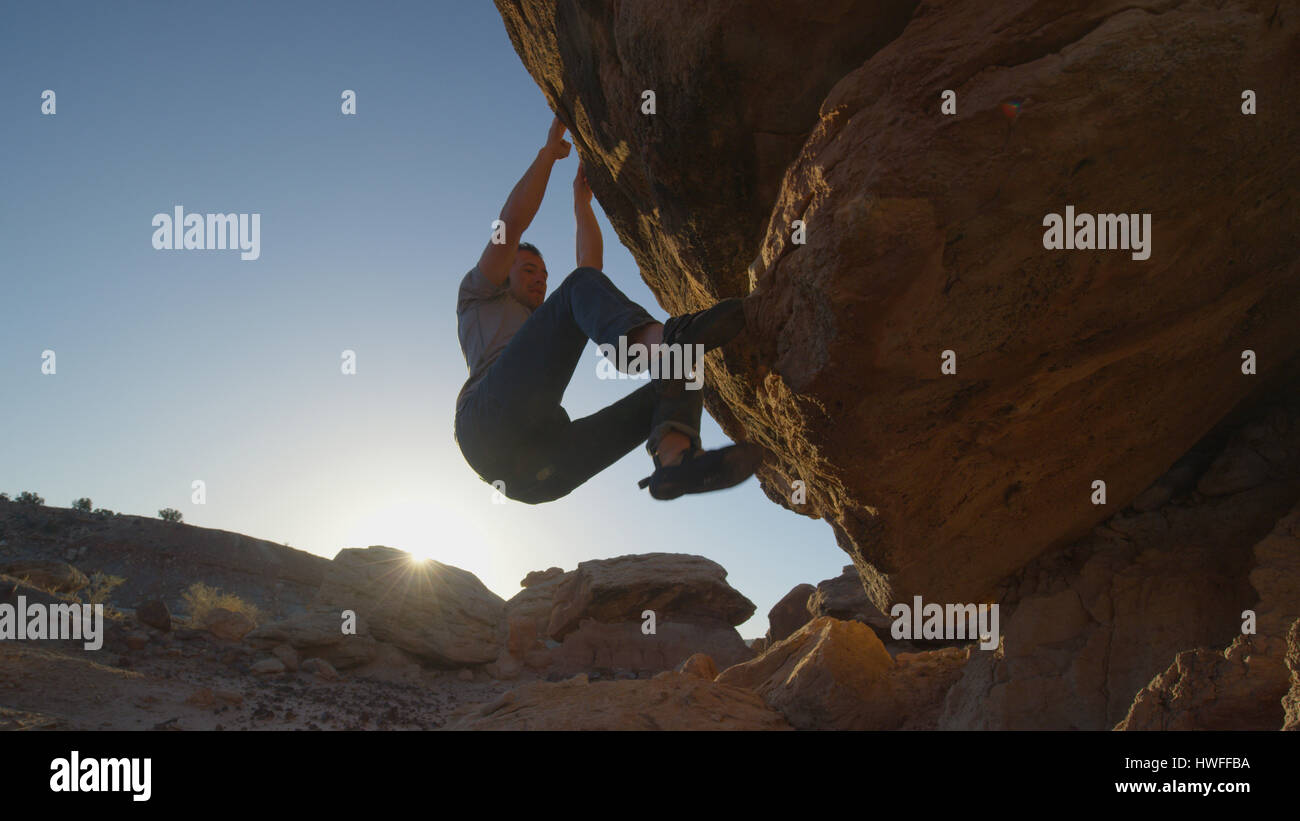 Low angle view of silhouette of climber clinging to steep rock cliff ...