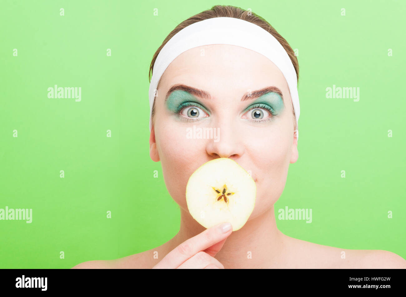 Young beautiful woman with a slice of apple in front of her mouth as ...