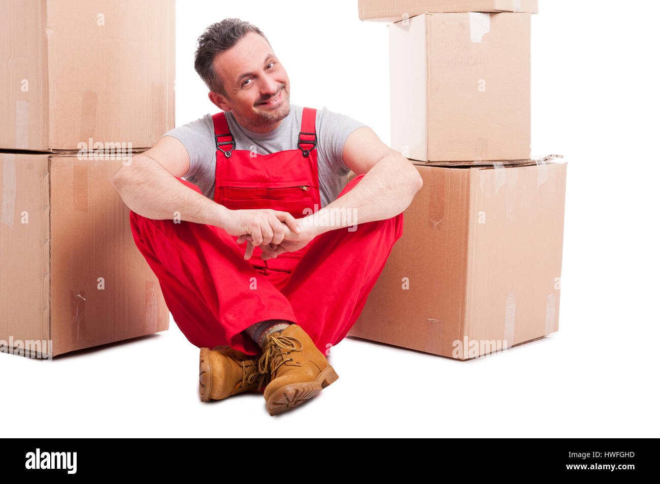 Mover man sitting on the floor surrounded by boxes and smiling isolated ...