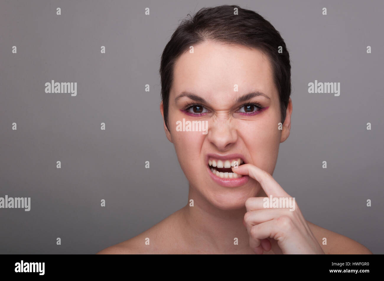 Angry or furious woman frowning and biting her finger on grey ...