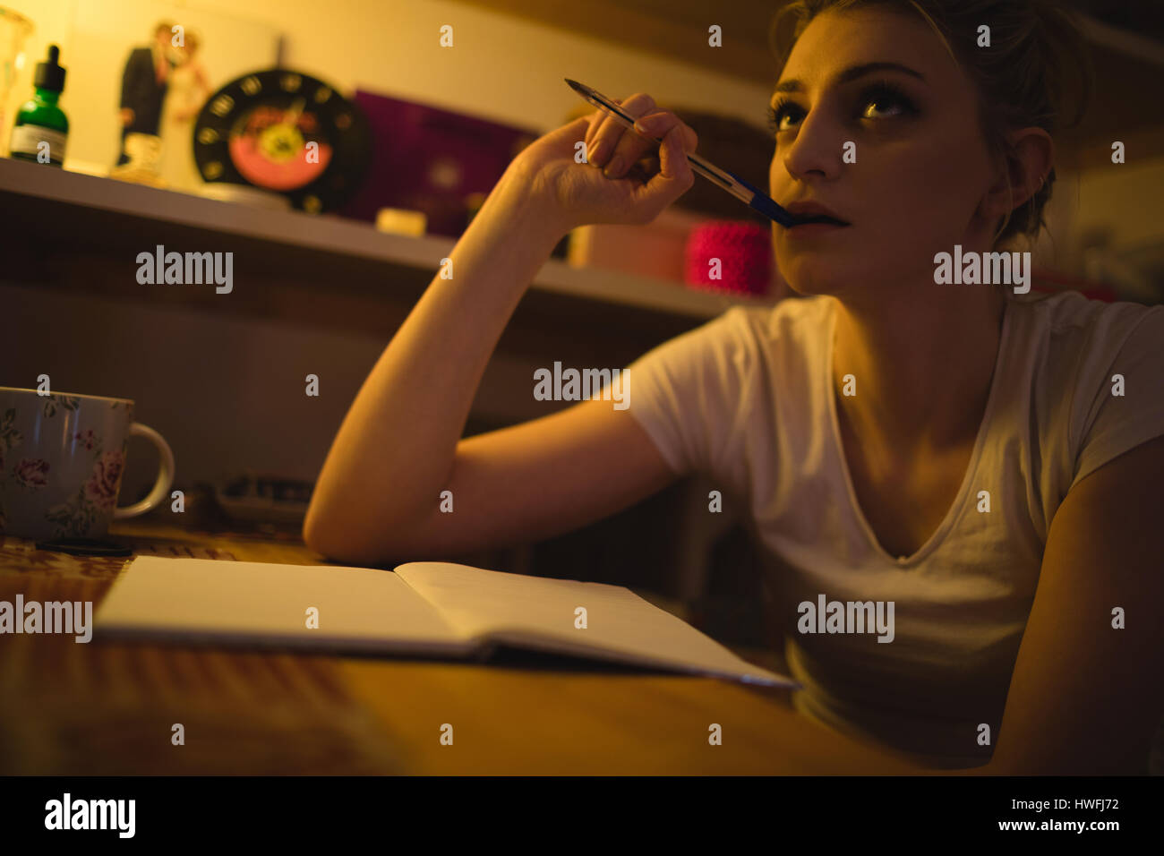 Woman thinking while writing notes in drawing room at home Stock Photo ...