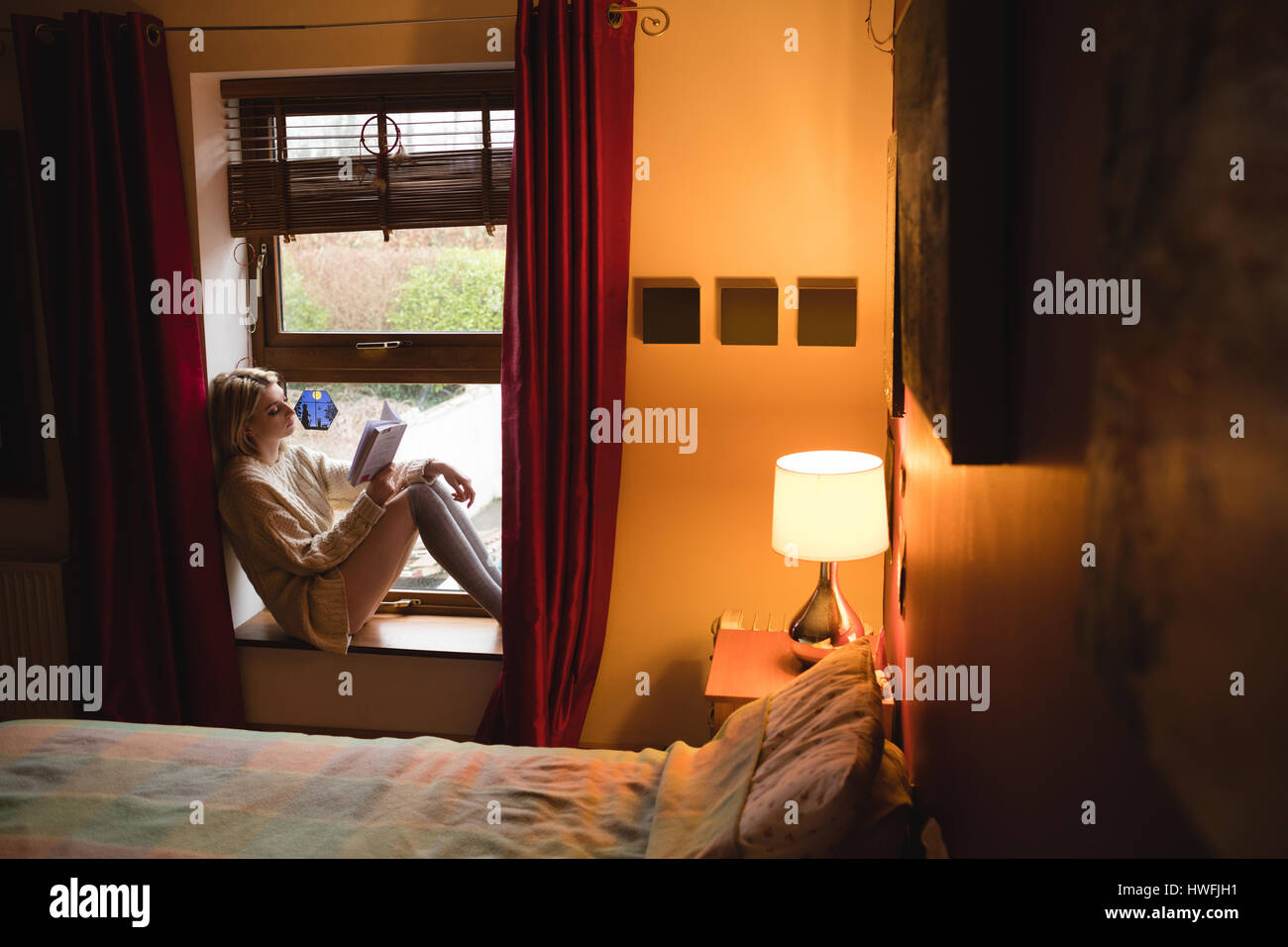 Woman sitting on window and reading a book at home Stock Photo - Alamy
