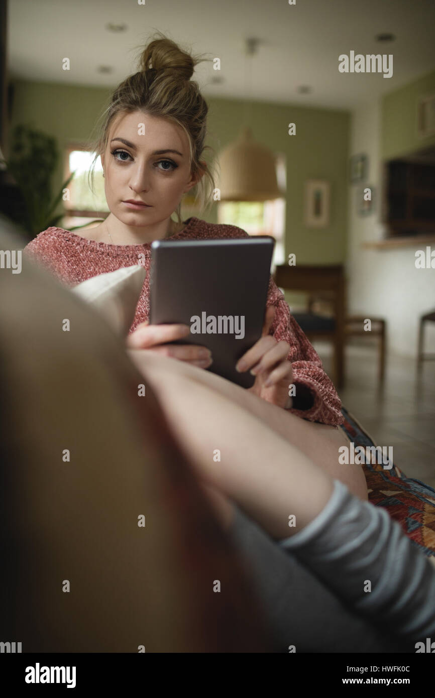 Woman sitting and using digital tablet on couch in living room at home ...