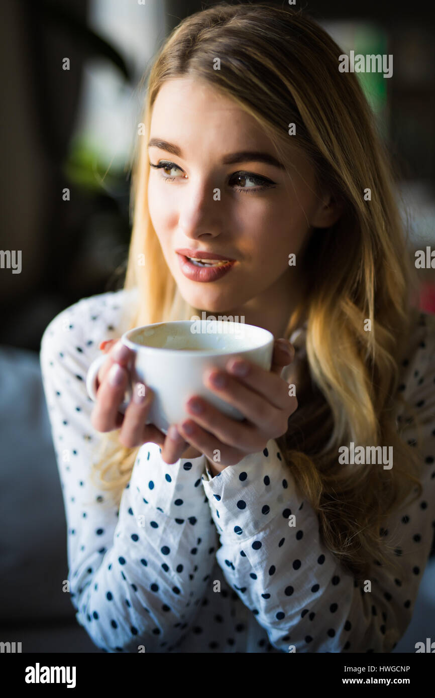 Portrait of young gorgeous female drinking tea and thoughtfully looking ...