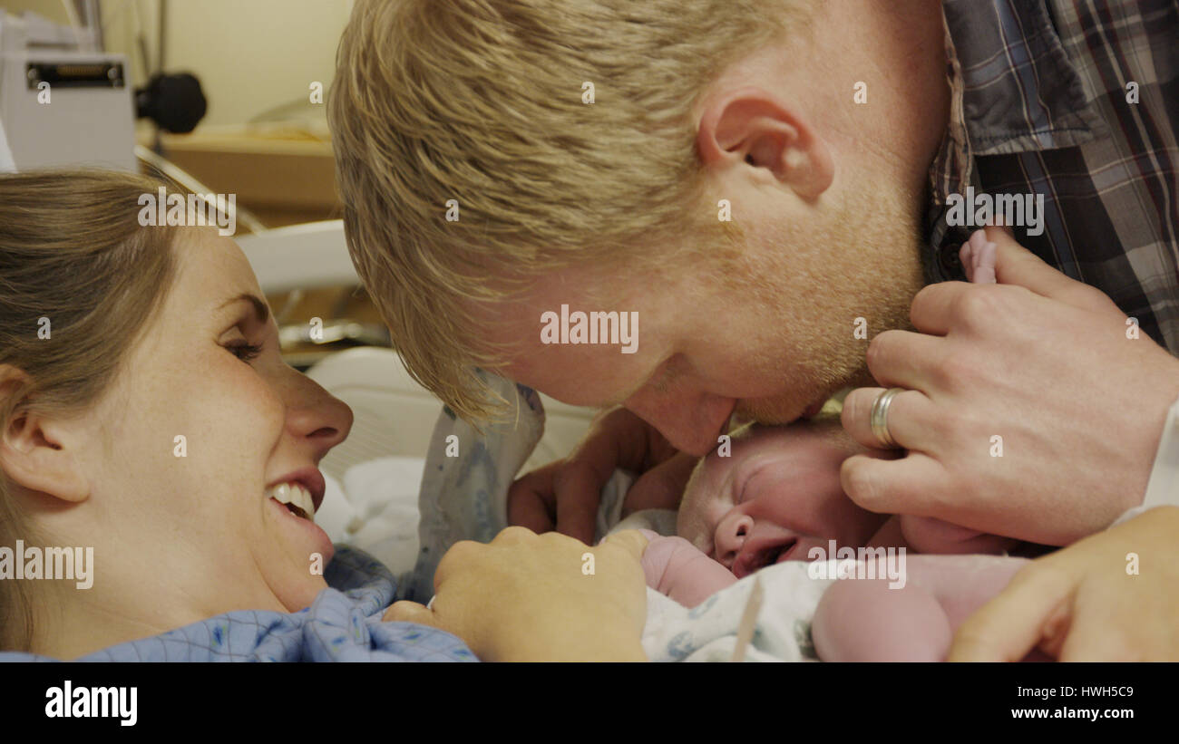 Profile view of new mother and father admiring newborn baby in hospital ...