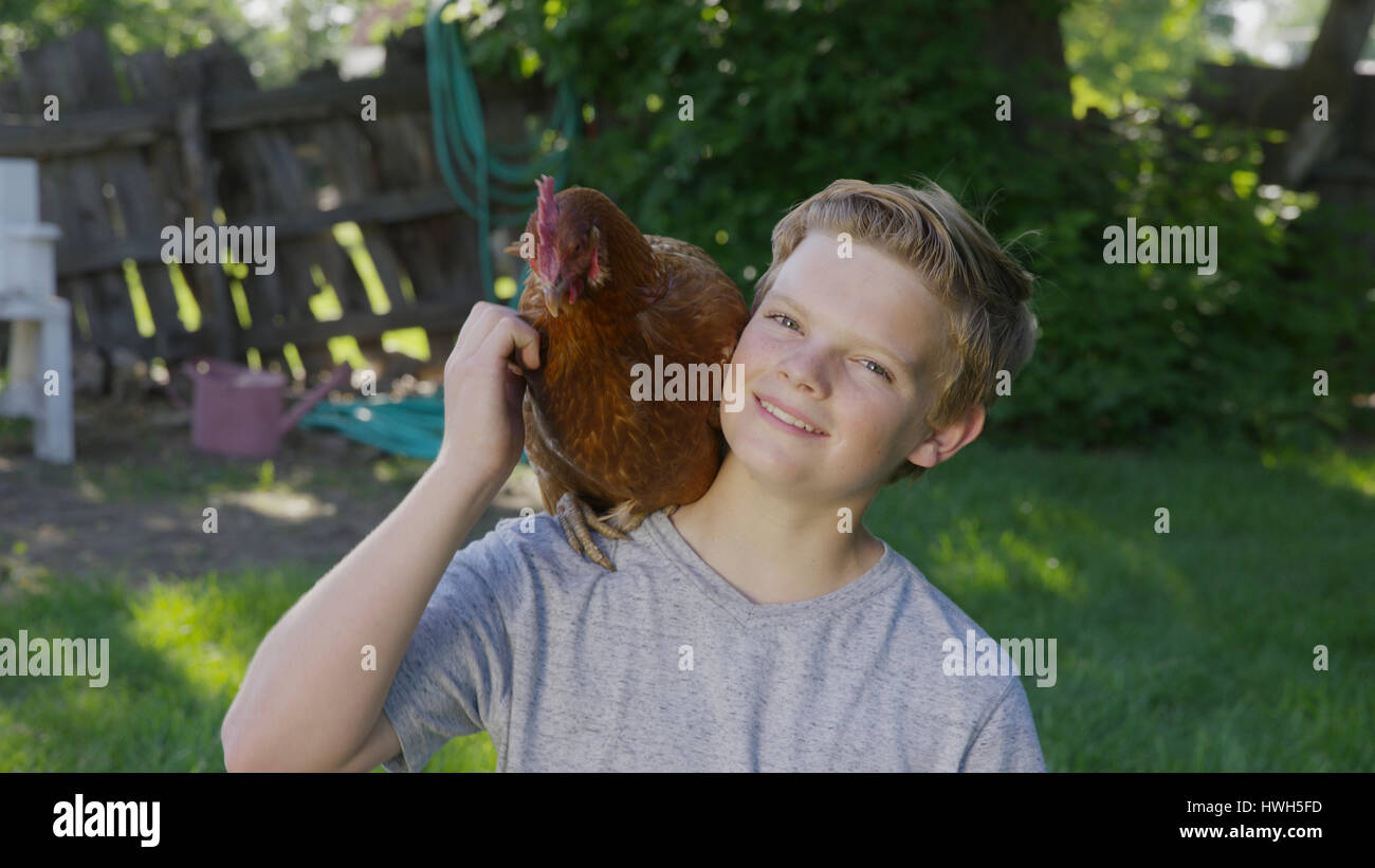 High angle portrait of smiling boy petting rooster on shoulder in ...