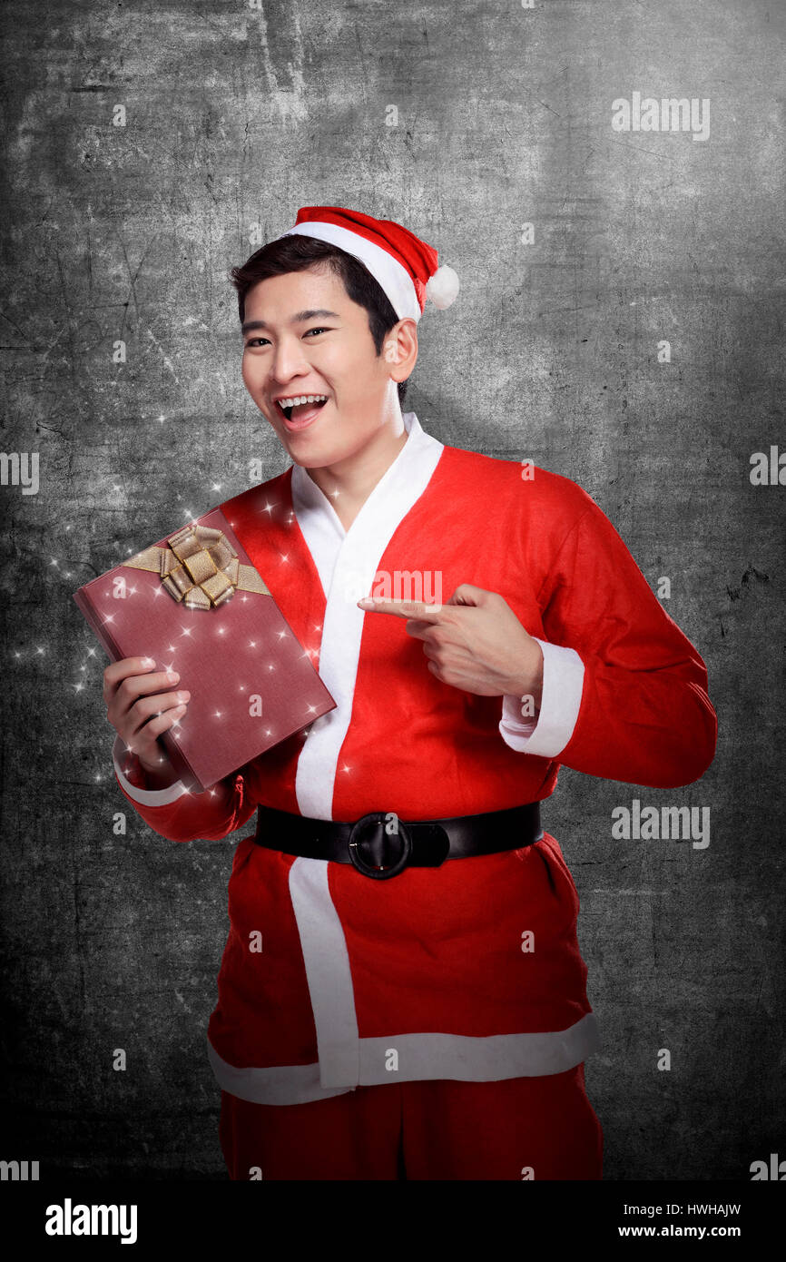 Handsome asian man wearing costume as santa claus, holding gift box ...