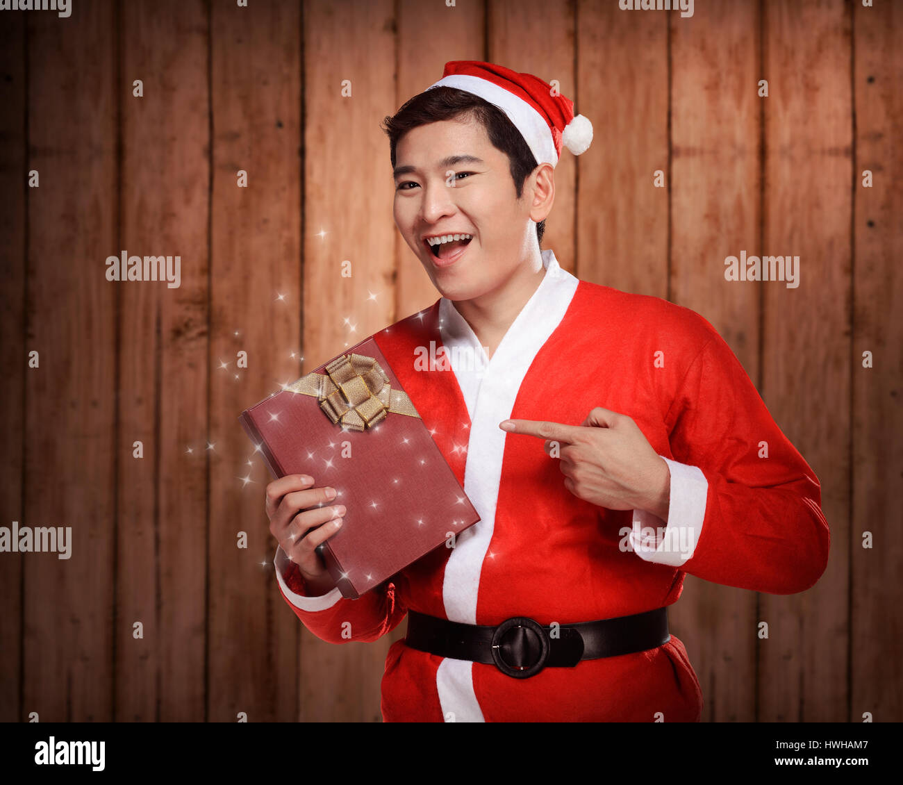 Handsome asian man wearing costume as santa claus, holding gift box ...