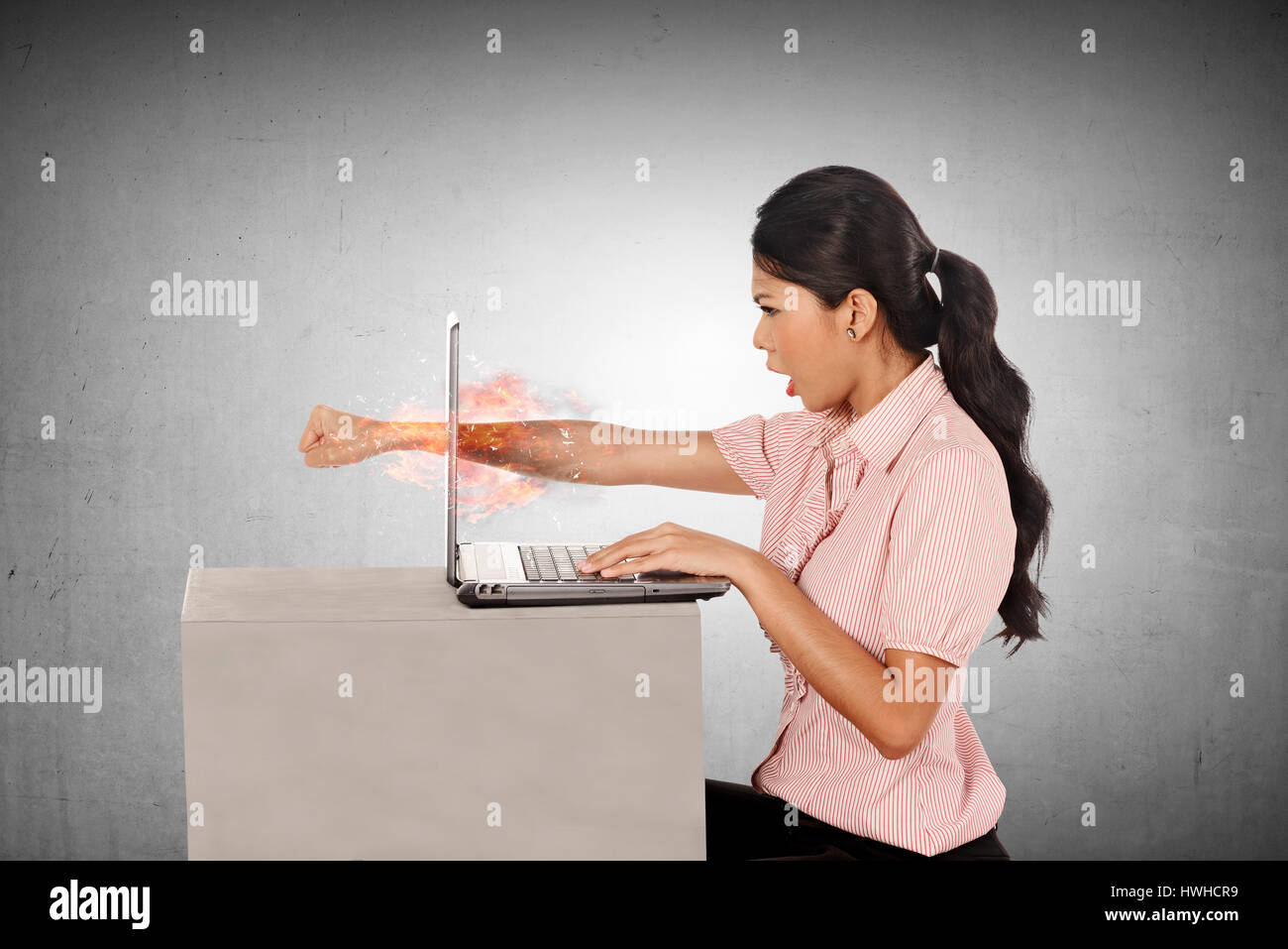 Furious asian business woman throws a punch into the laptop on grey ...