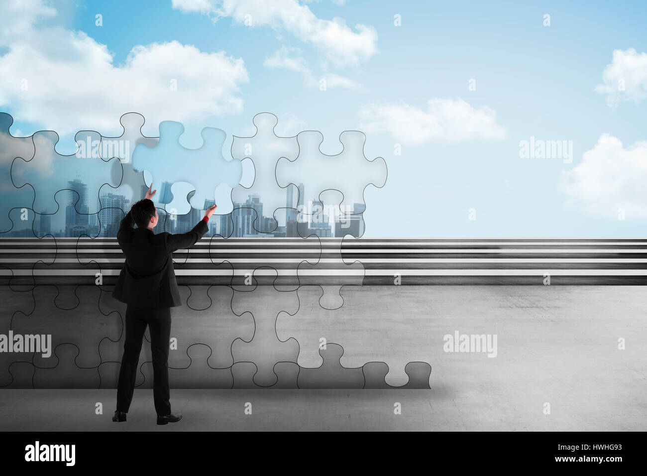 Asian business man holding piece of puzzle trying to build a city ...