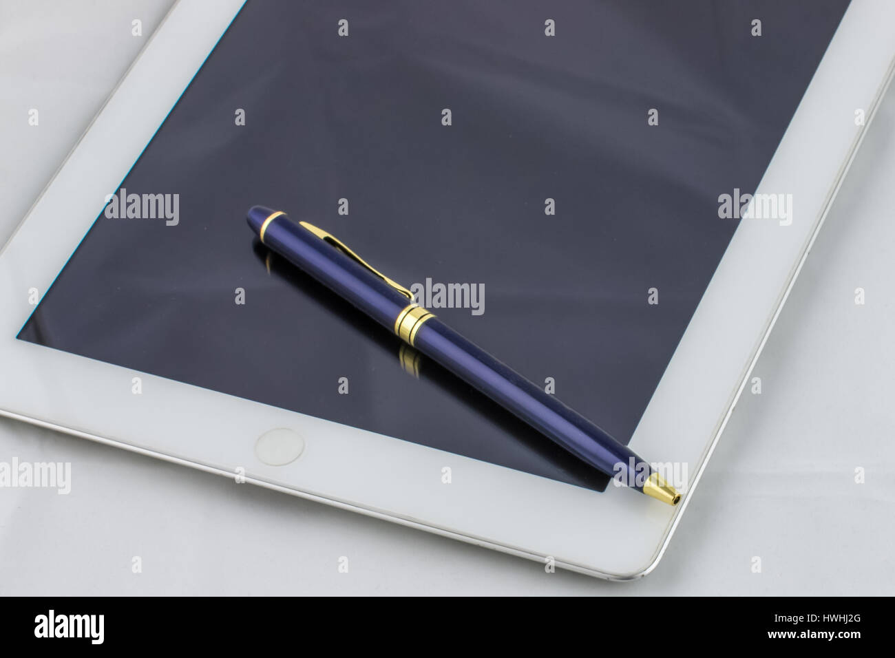 Tablet computer and pen from above is reflected in glass on white ...