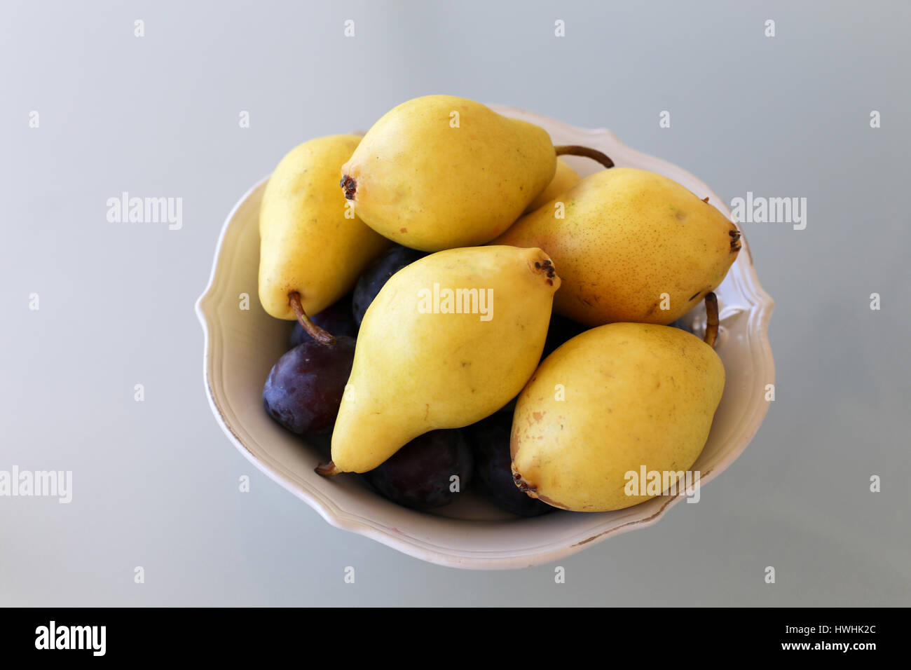 Big yellow pears and plums in white round table centered on white glass ...