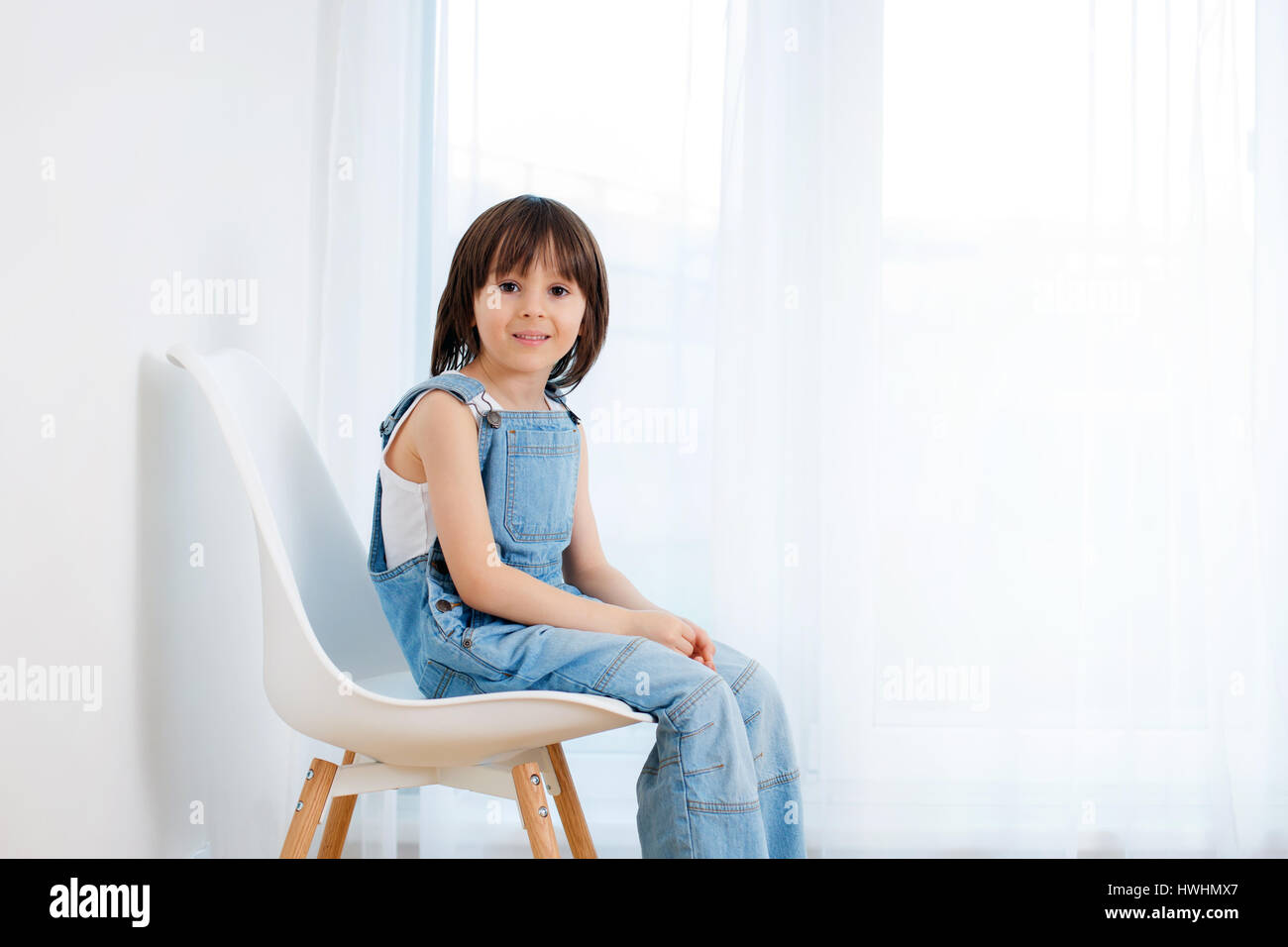 Cute child, sitting on white chair at home, isolated on white, looking ...