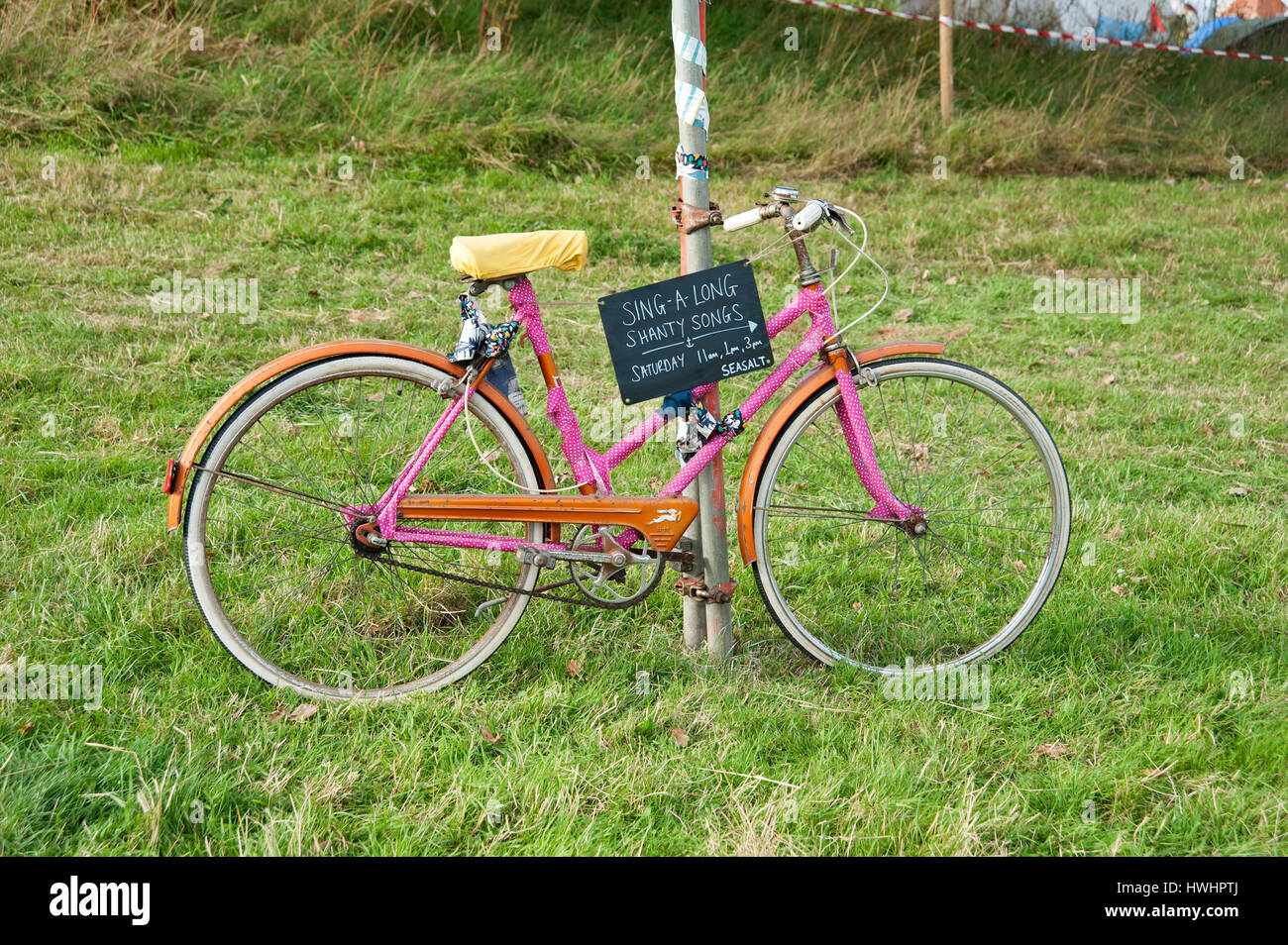 A push bike painted pink and decorated with festival signs in a field ...