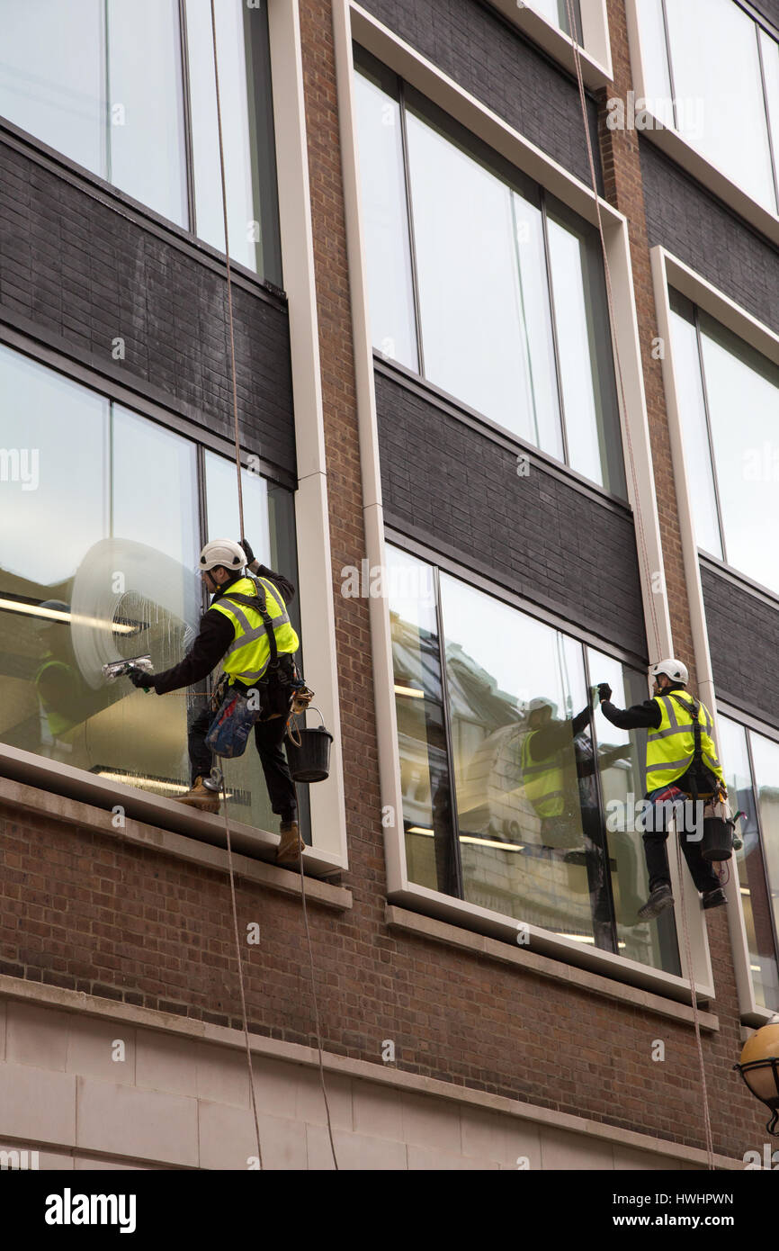 Two window cleaners working while abseiling down a new office block in ...