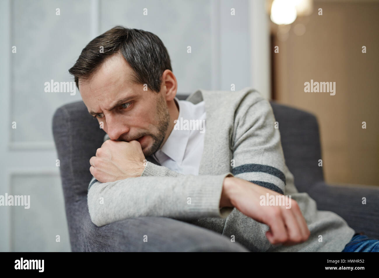 Nervous middle-aged man sitting on comfortable armchair and biting his ...