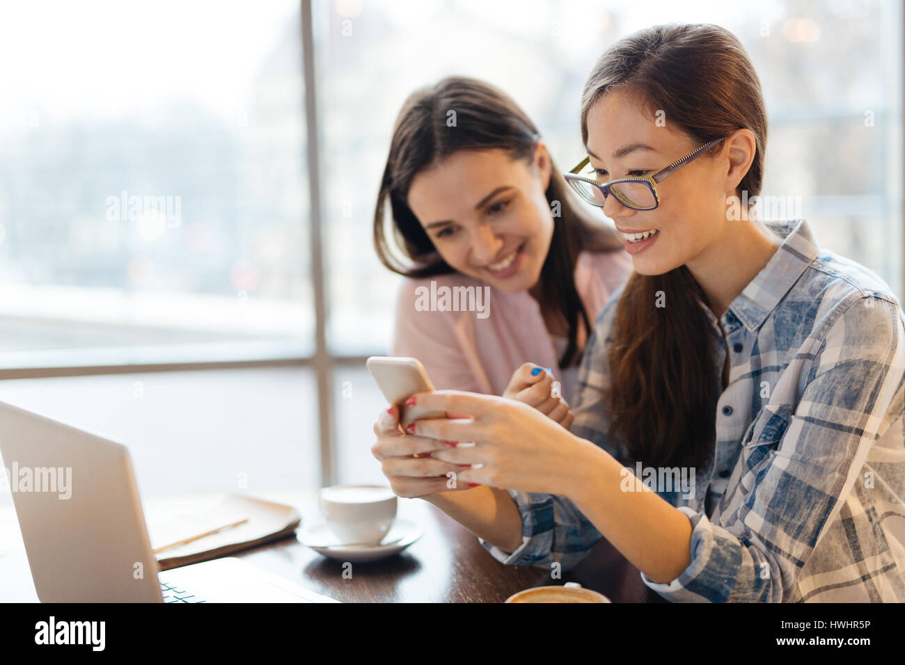 Girl with smartphone and her curious friend reading message Stock Photo ...