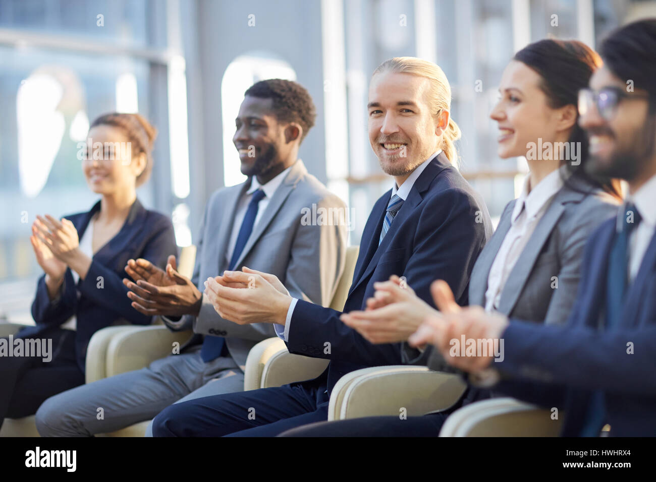 Multi-ethnic group of smiling business people sitting in row in modern ...