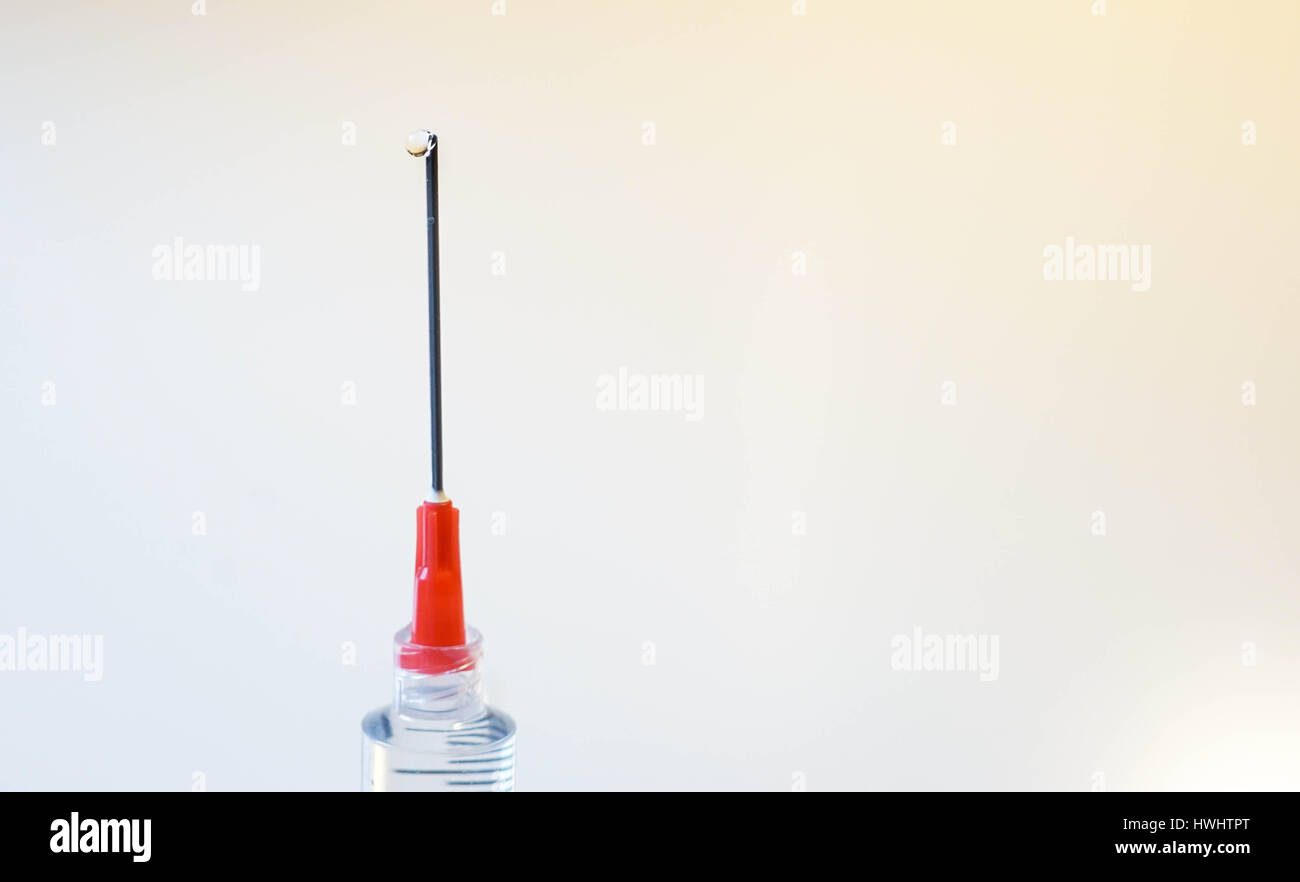 A syringe needle is help vertically and a drip of fluid exits and runs ...