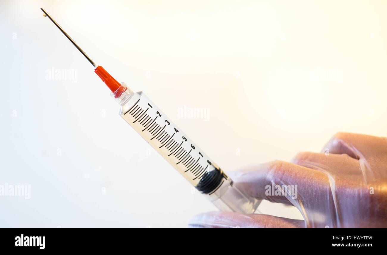 A full syringe drips while a latex-gloved hand prepares to give an ...