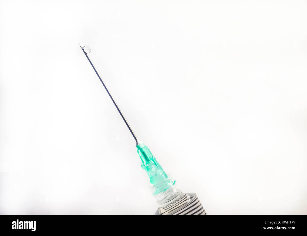 A diagonally held medical syringe with a green tip is dripping fluid ...