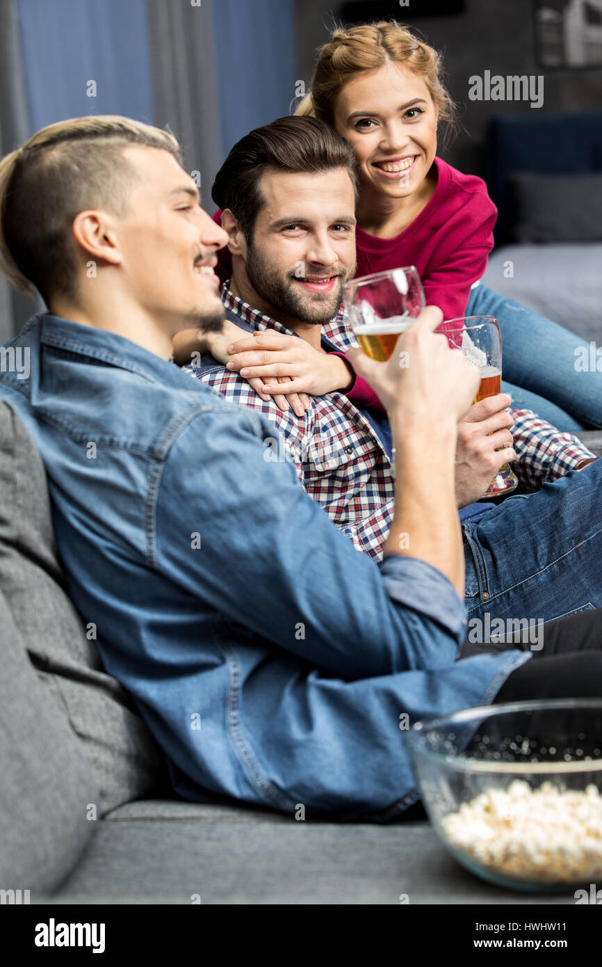 Happy young friends sitting on couch and drinking beer Stock Photo - Alamy