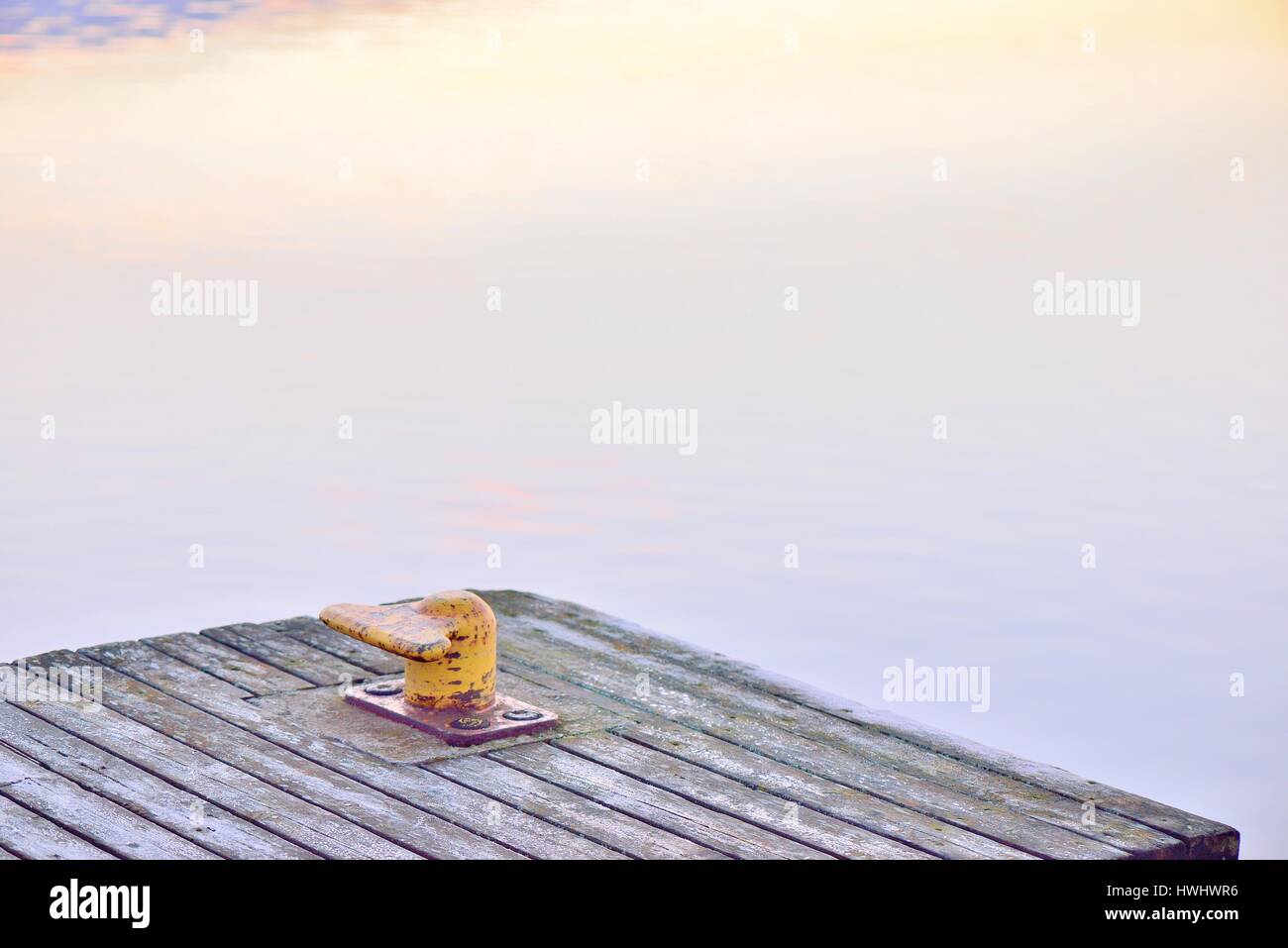 Yellow bollard, or a harbor post, on a wooden pier. Rust seen on the ...