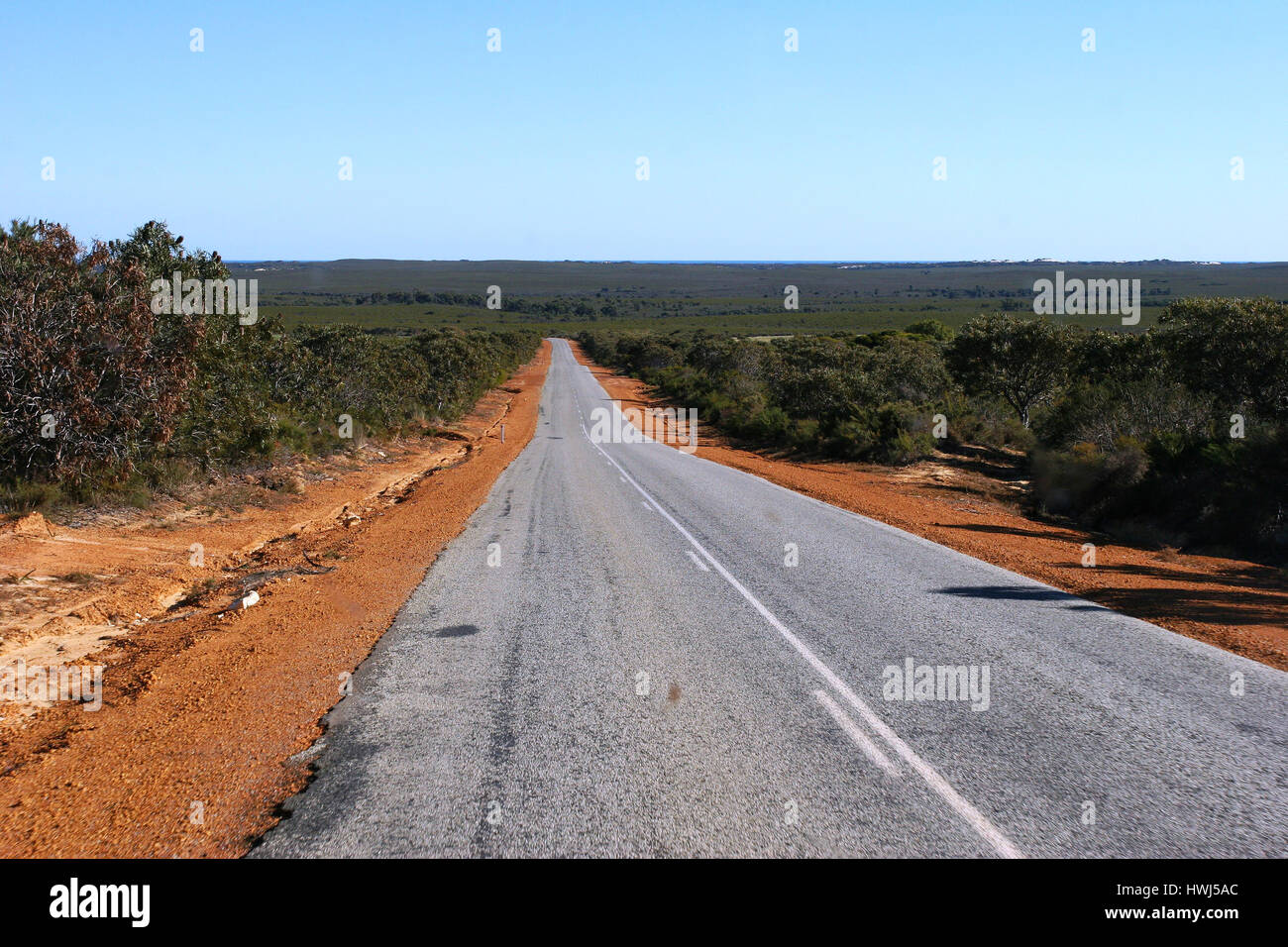 Sealed outback road lined with red earth and bushed leading towards ...