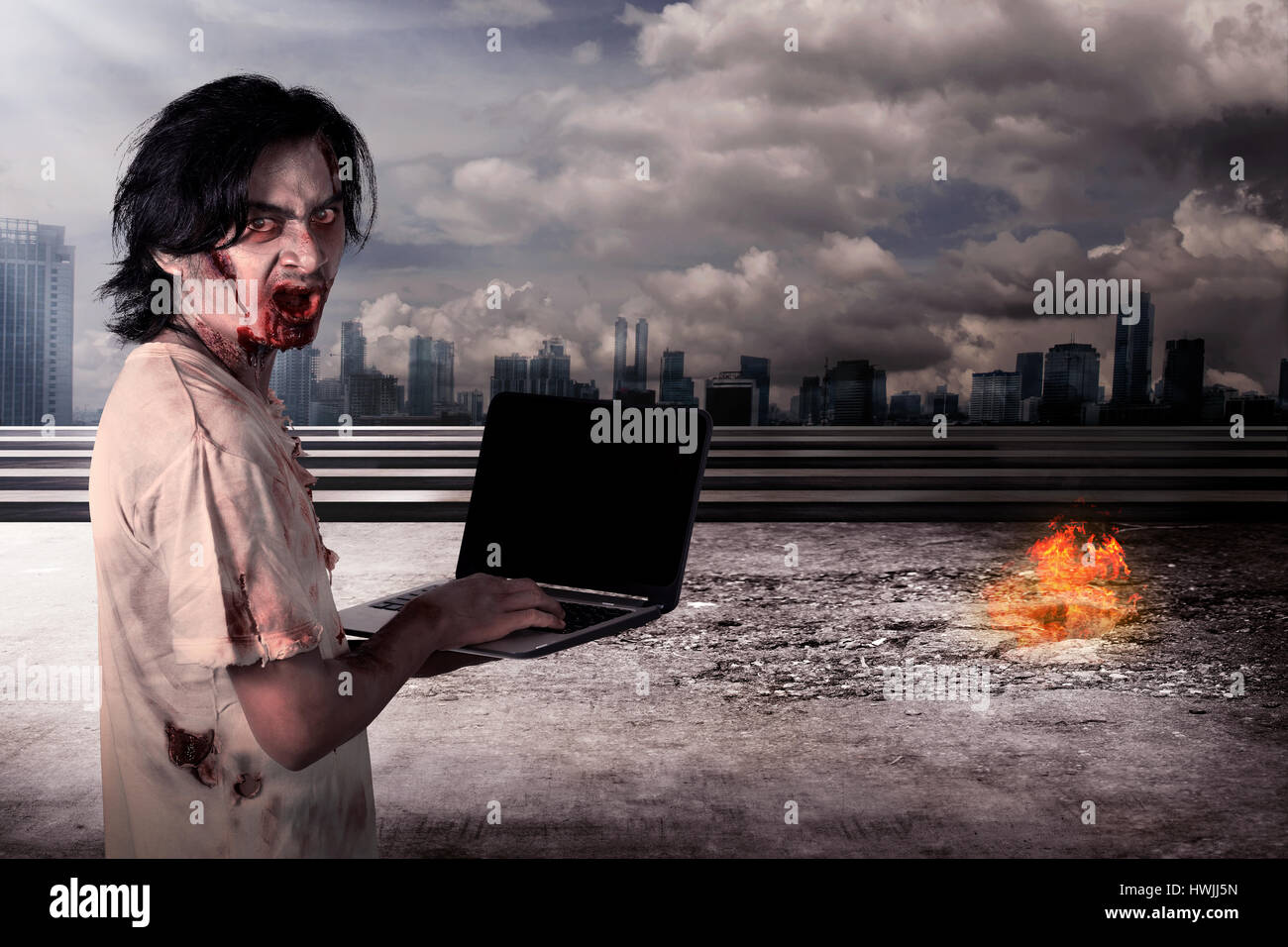 Creepy male zombie typing with laptop with city on fire background ...